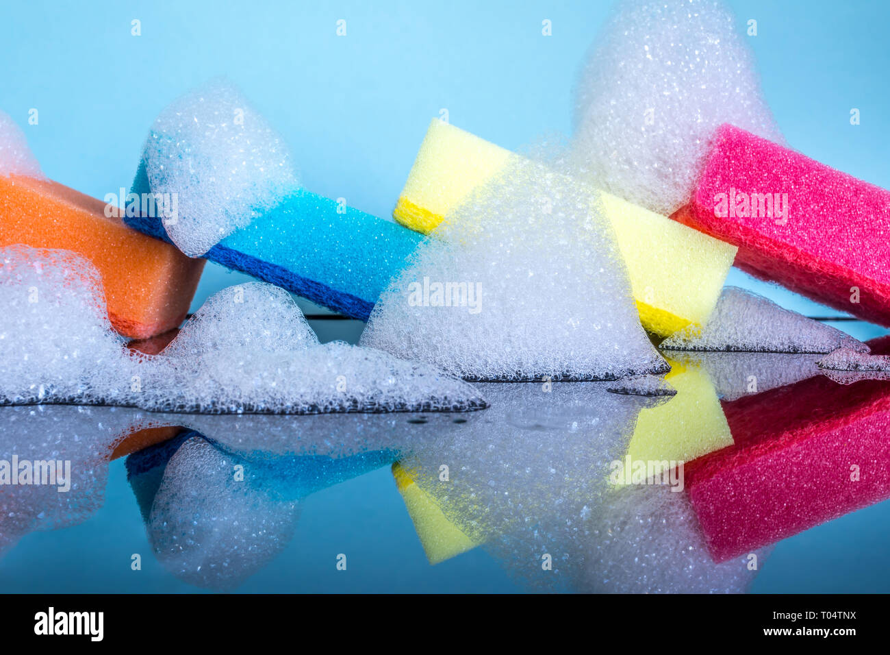 Colorful sponges with foam and reflection close-up on a blue background ...