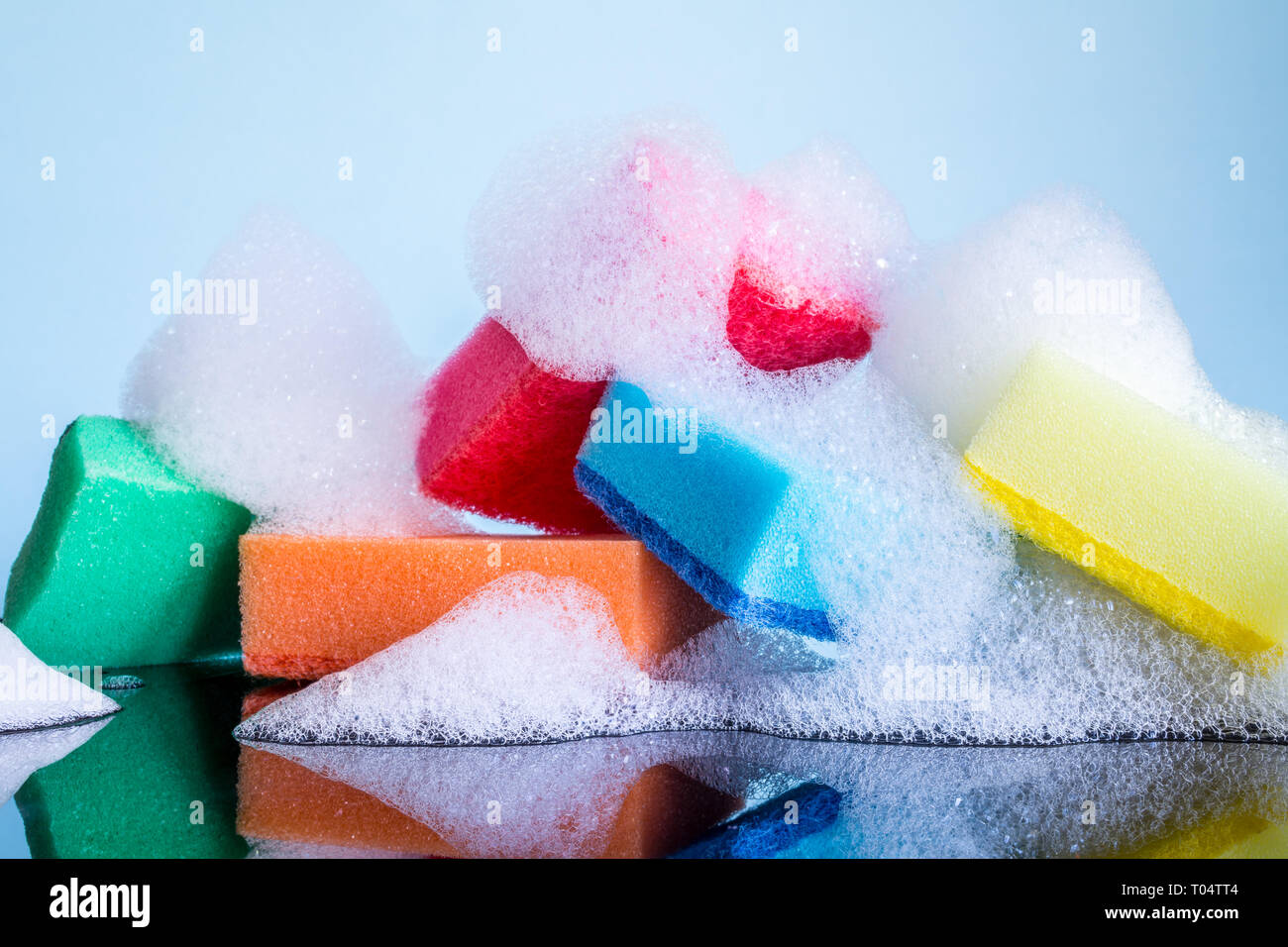 Colorful sponges with foam and reflection close-up on a blue background ...