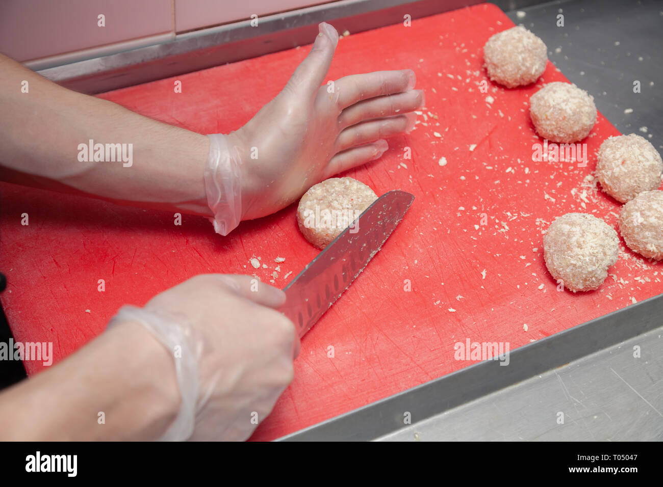 Chef's hands in gloves creating forming chicken cutlets with knife for ...