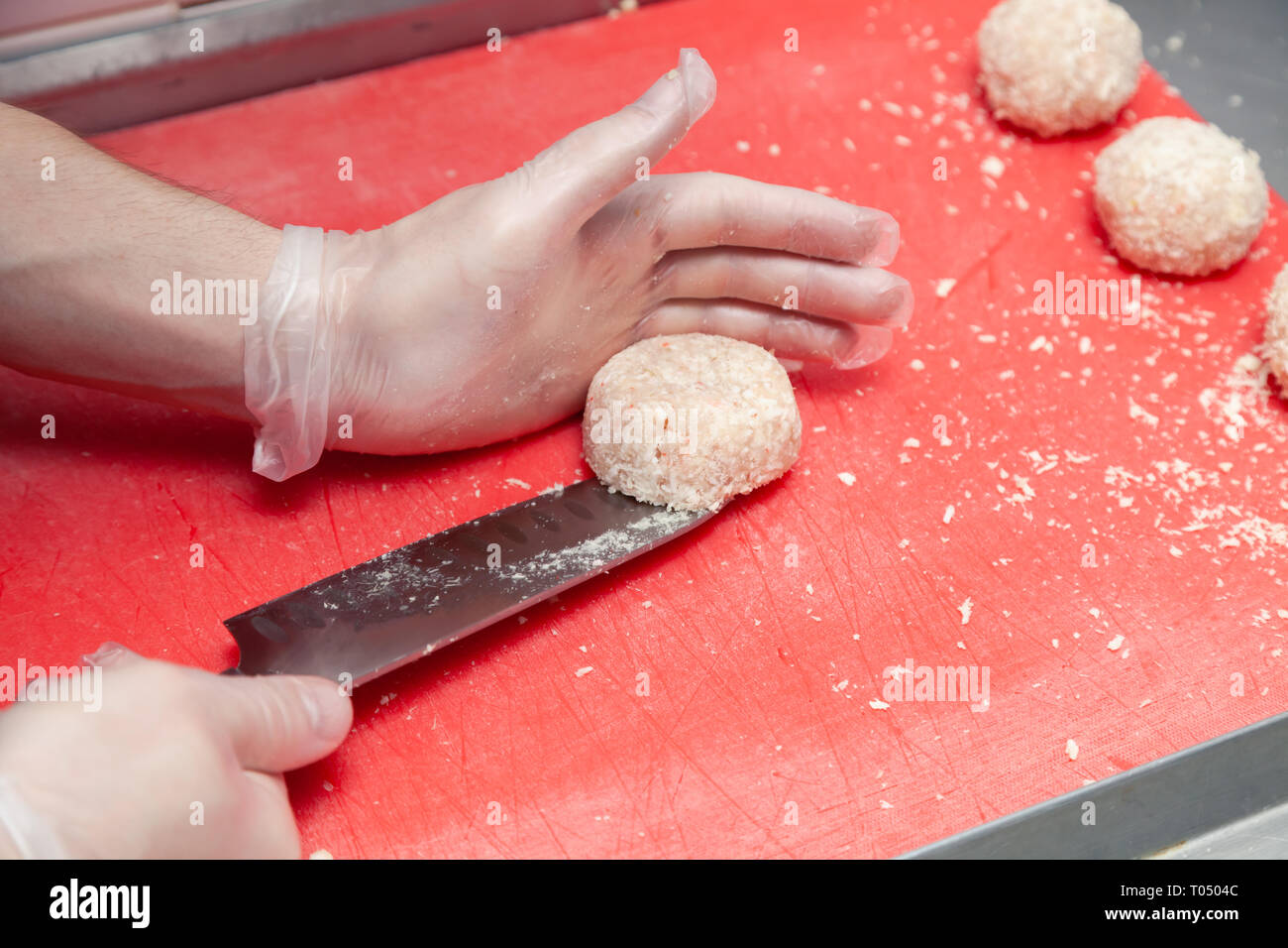 Chef's hands in gloves creating forming chicken cutlets with knife for ...