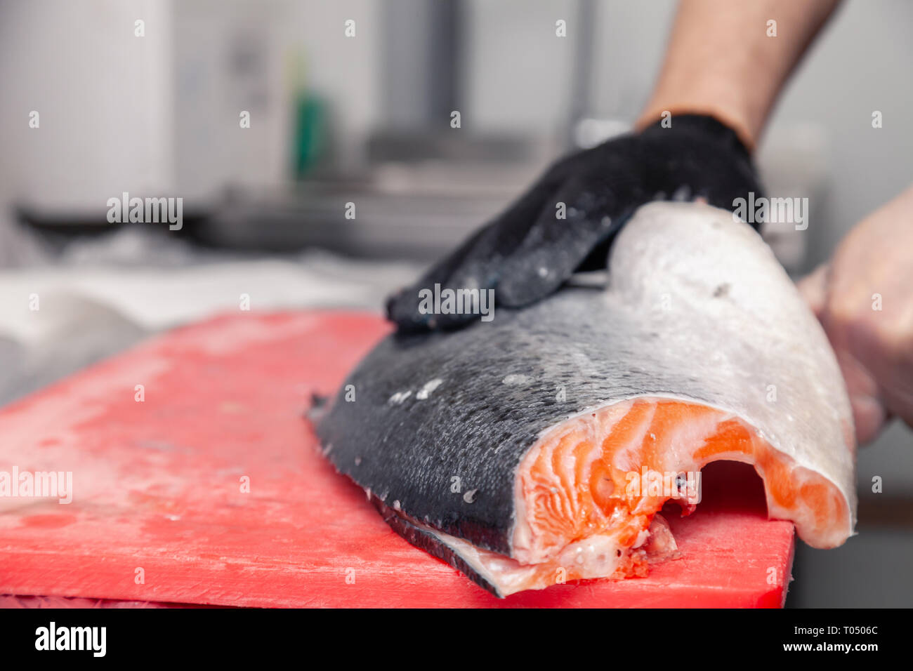 Chef cook carving whole fresh norwegian salmon fish with knife on red ...