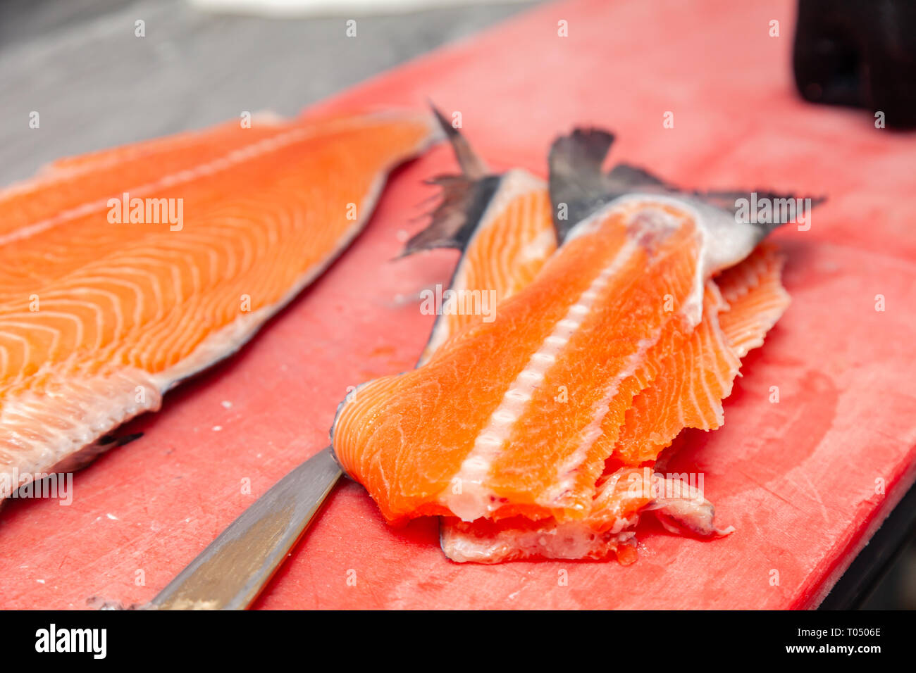 Closeup carving whole fresh norwegian salmon fish with knife on red ...