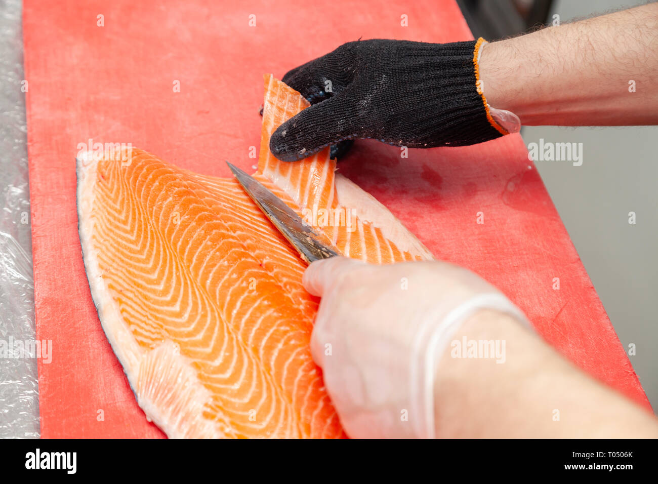 Chef cook carving whole fresh norwegian salmon fish with knife on red ...