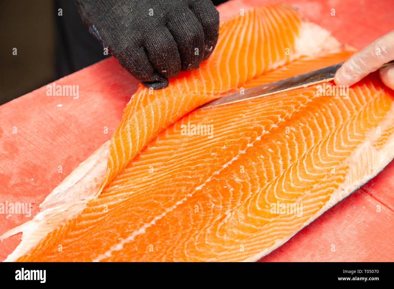 Chef cook carving whole fresh norwegian salmon fish with knife on red ...