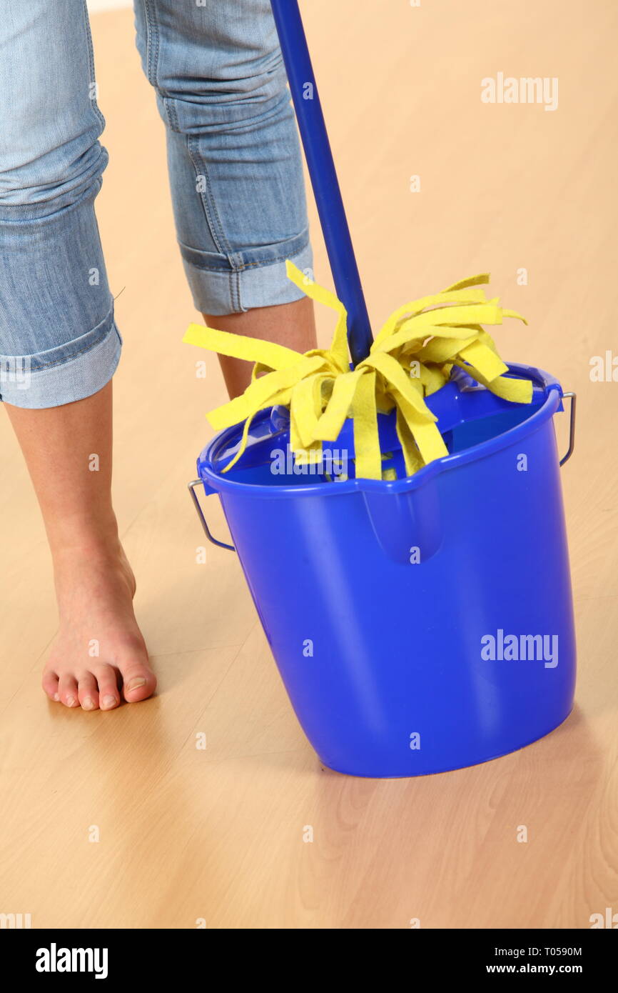 A woman stands barefoot in front of a cleaning bucket. Only her legs ...