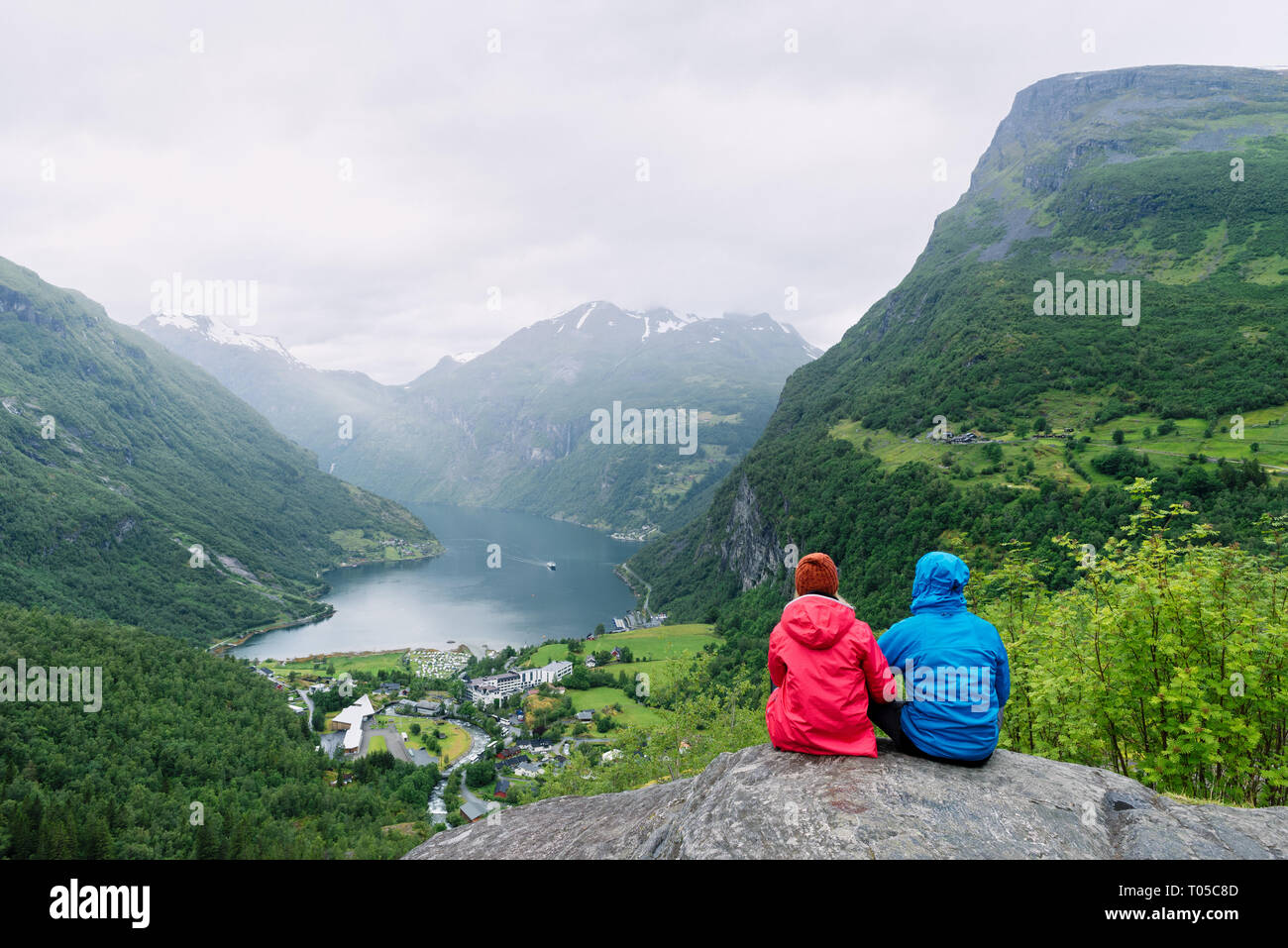 Couple sitting on a rock with look at the fjord and mountains. Tourist ...