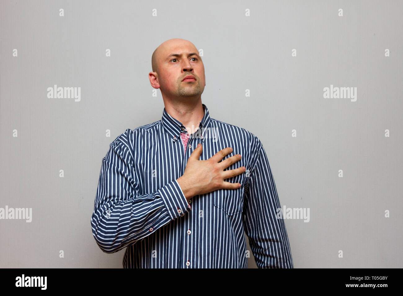 The bald man put his hands on his chest. On a gray background Stock ...