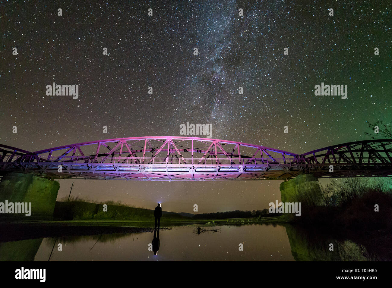Back view of man with flashlight standing on river bank under ...