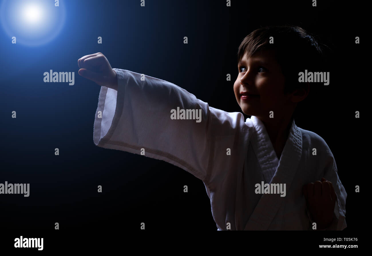 Cute karate boy in white kimono isolated on dark background. Child ...
