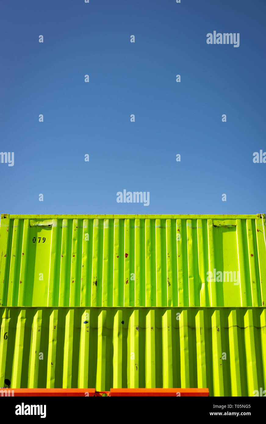 A stack of colorful green shipping containers against a blue sky ...