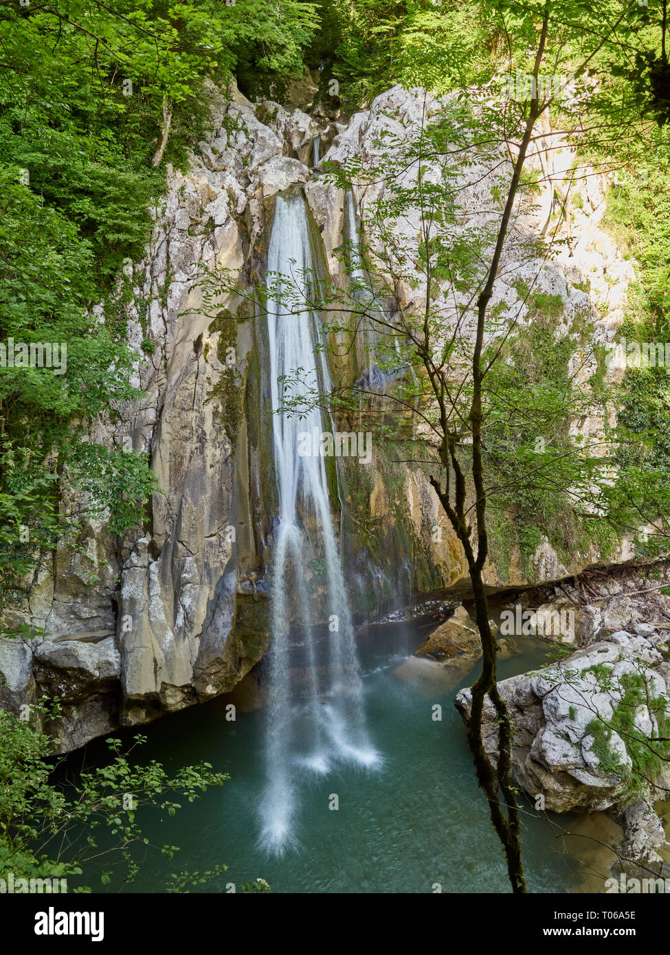 A high waterfall falls from a cliff into a clear lake. The waterfall is ...