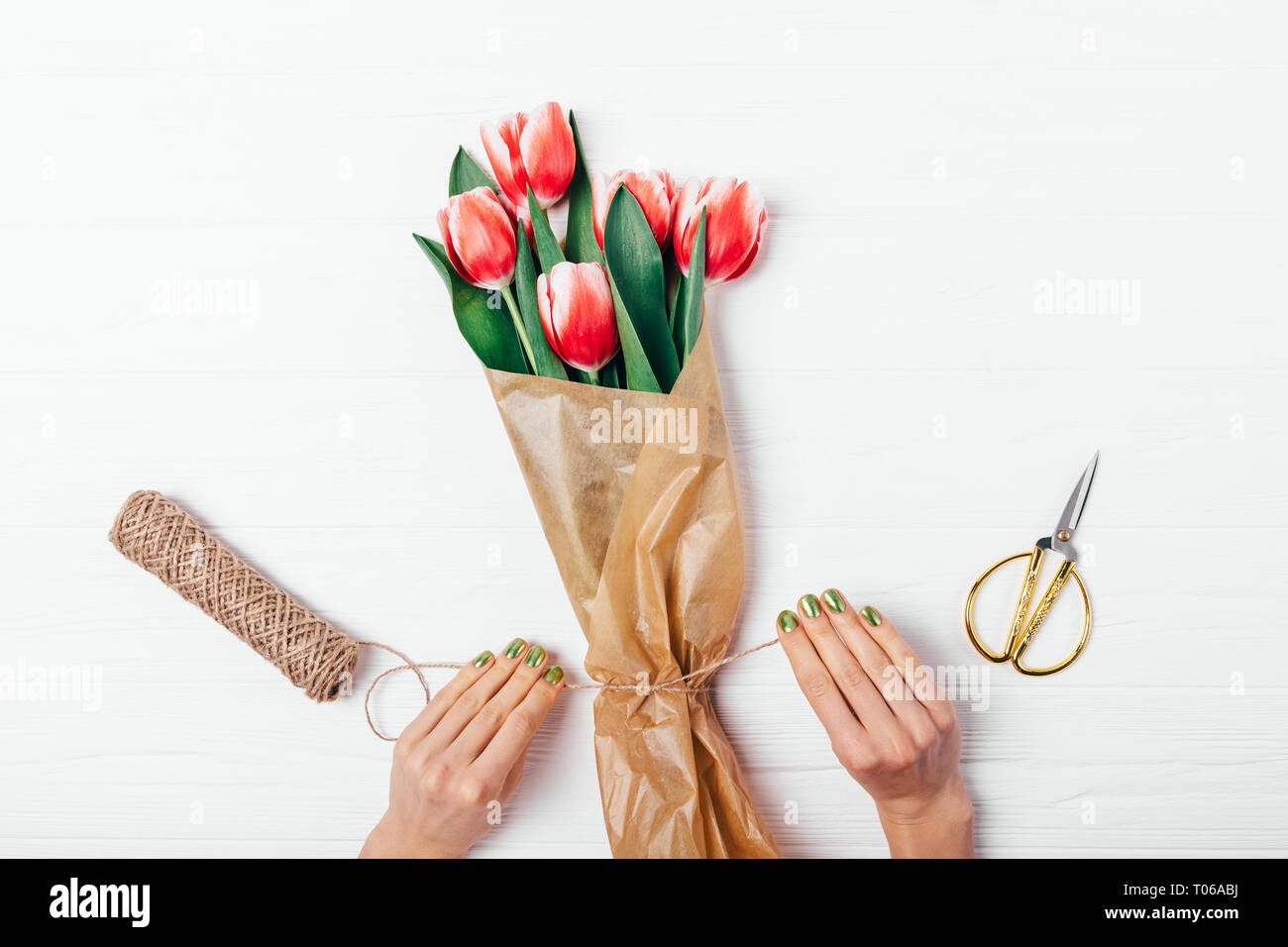Female's hands wrapping bouquet of fresh red tulip flowers in kraft ...