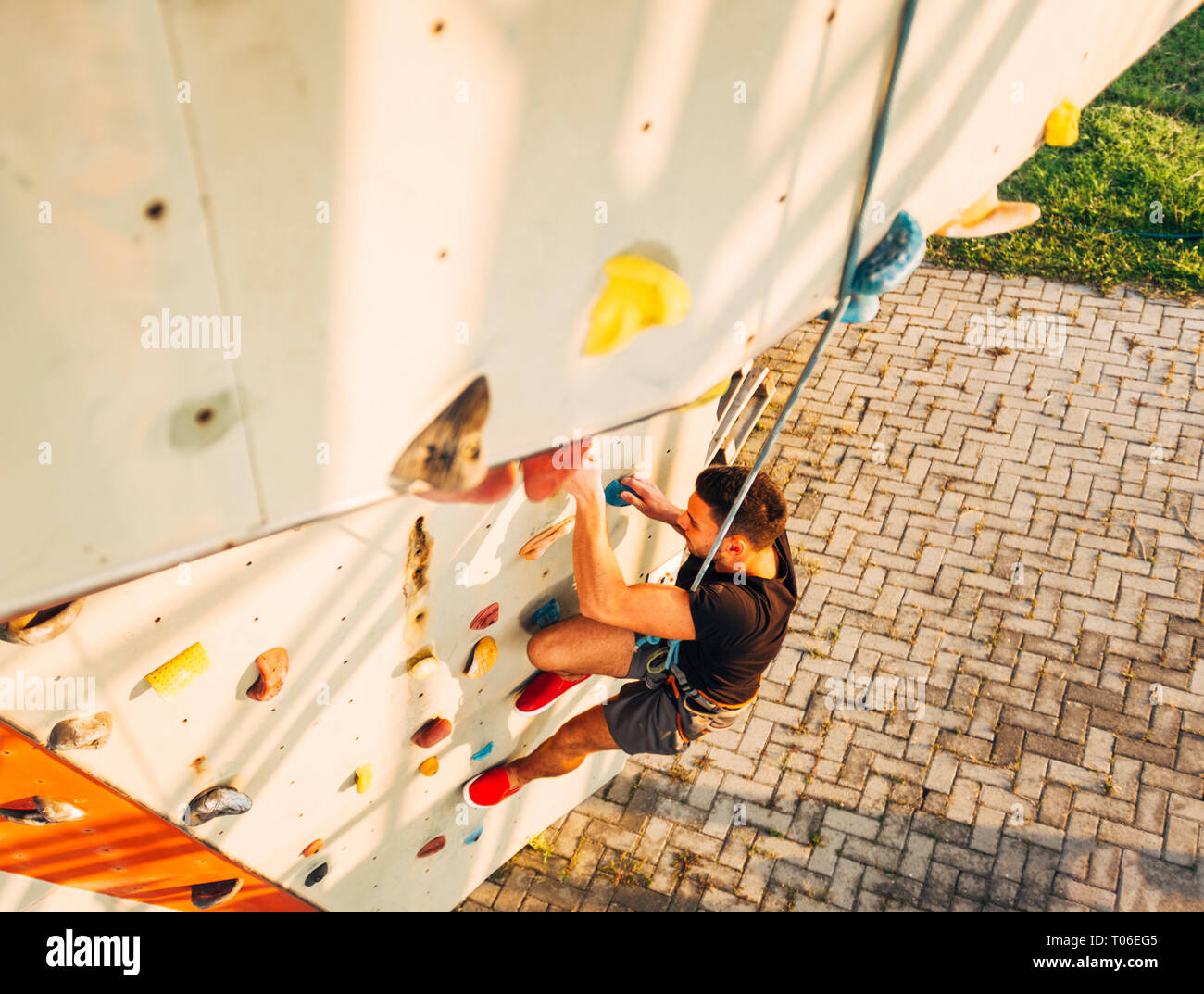 Man wearing belaying rope, climbing on a very high rock climbing wall ...