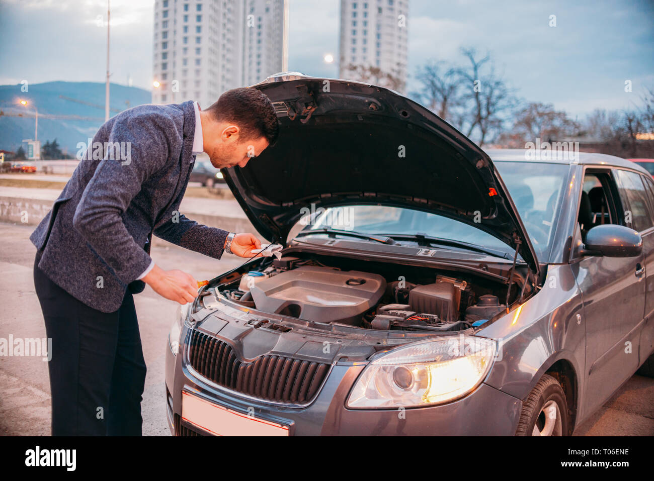 A tired worker is standing next to his car formally dressed and looking ...