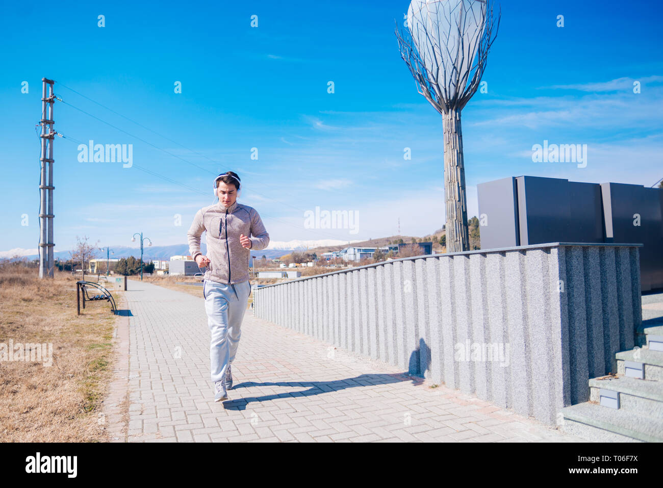 A panting athlete running fast on a track while wearing headphones and ...
