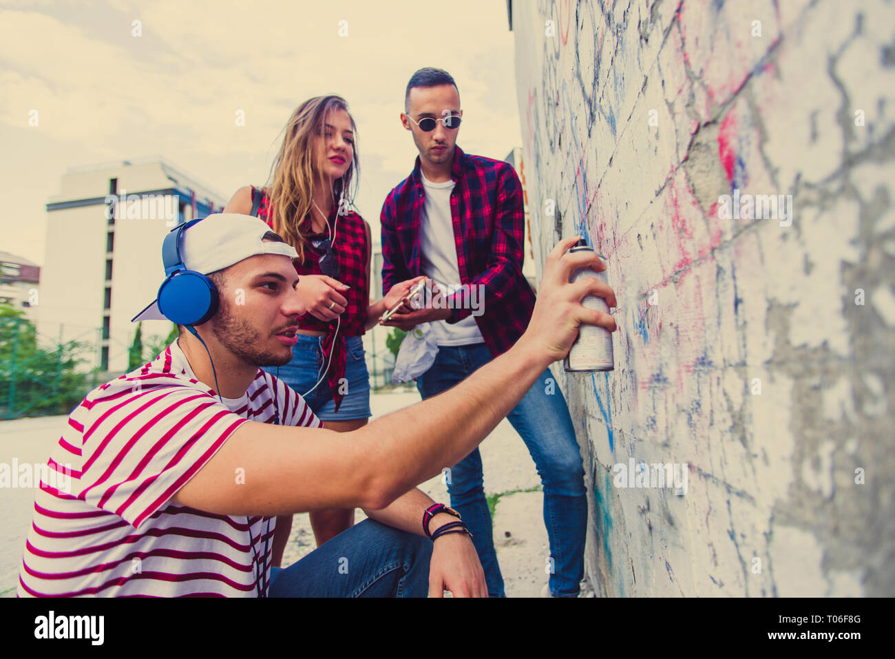 Three young friends having fun while drawing graffiti on the wall with ...