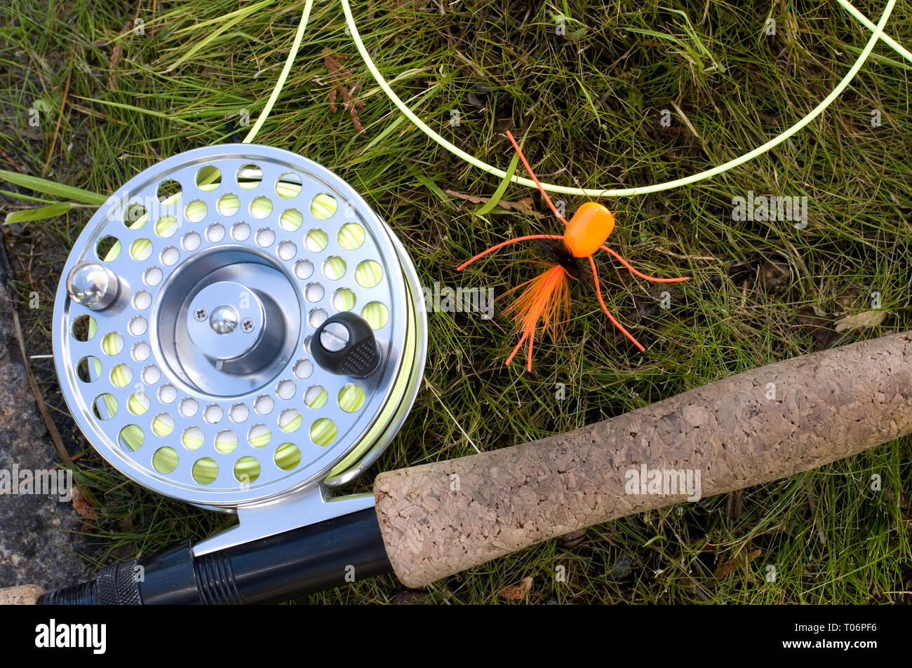 Fly fishing Rod and Reel with Orange Spider Lure on Wet Grass Stock ...