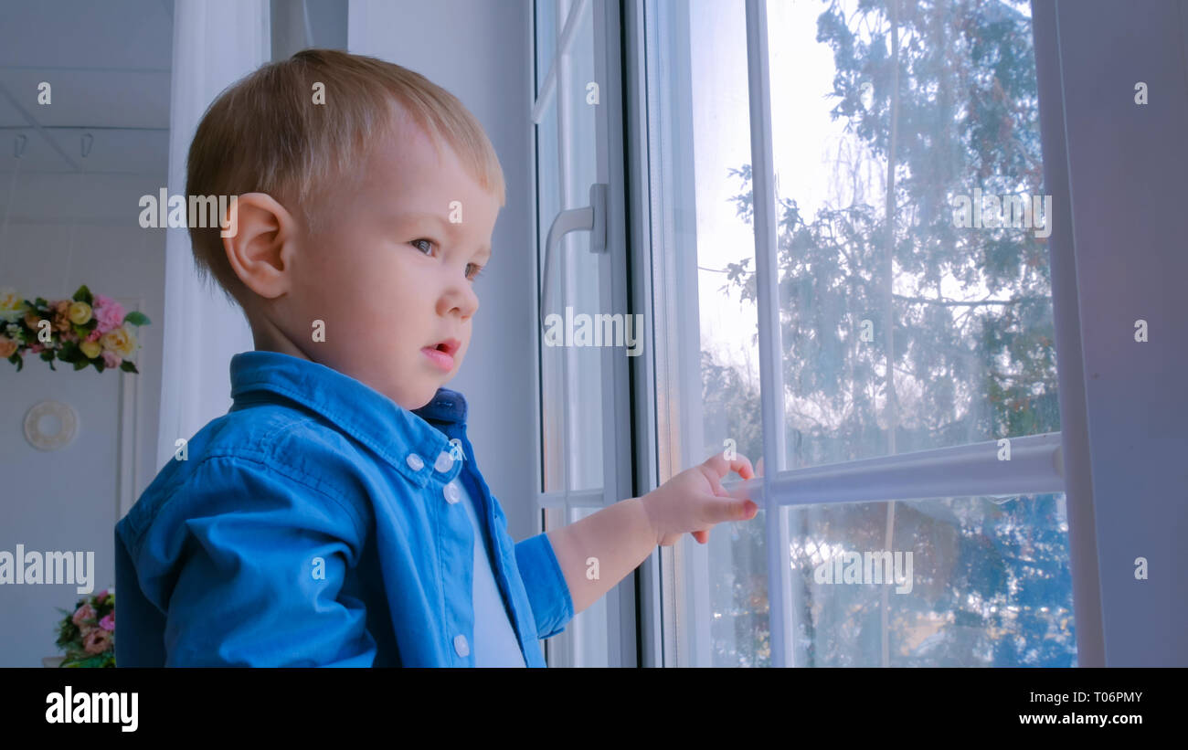 Pensive little boy looking through window Stock Photo - Alamy
