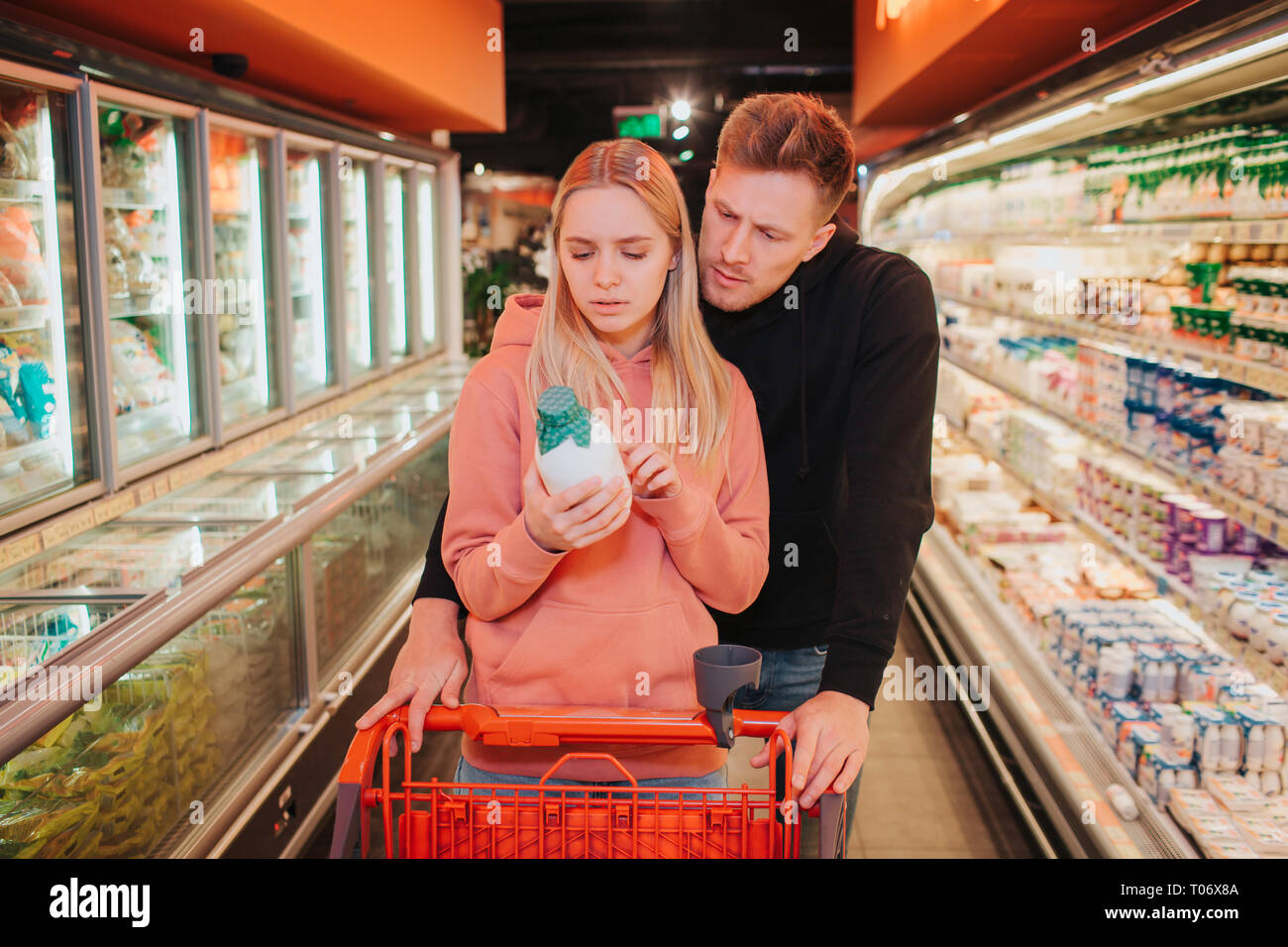 Young couple in grocery store. Careful people read ingredients on milk ...