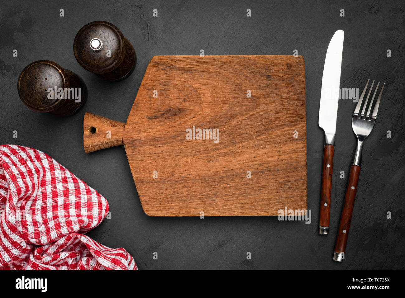 Cutting board, cutlery and plaid kitchen napkin on black concrete ...