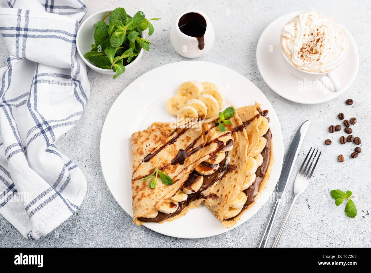Crepes with banana, chocolate and cup of cappucino on concrete ...