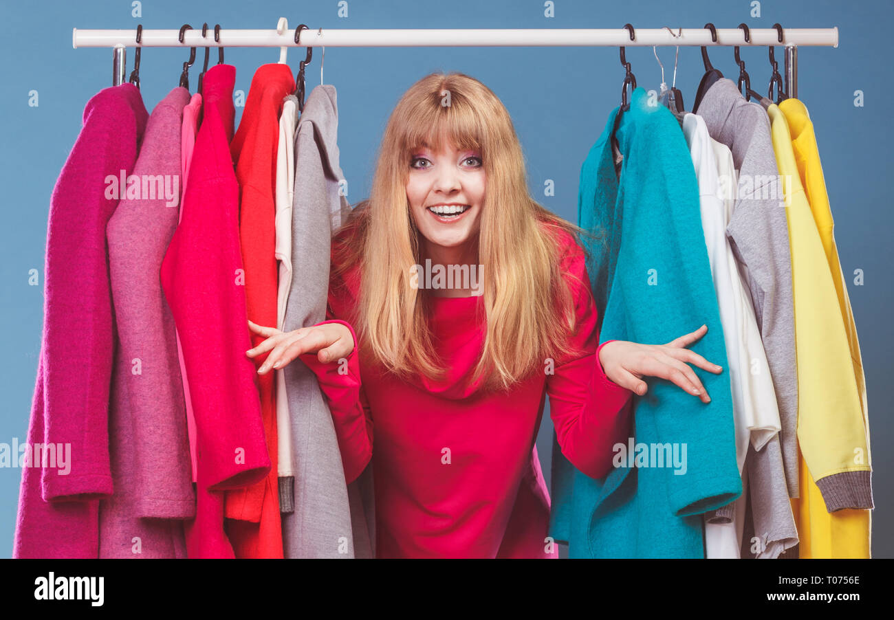 Happy smiling pretty woman choosing clothes to wear in wardrobe. Gorgeous young girl customer ...