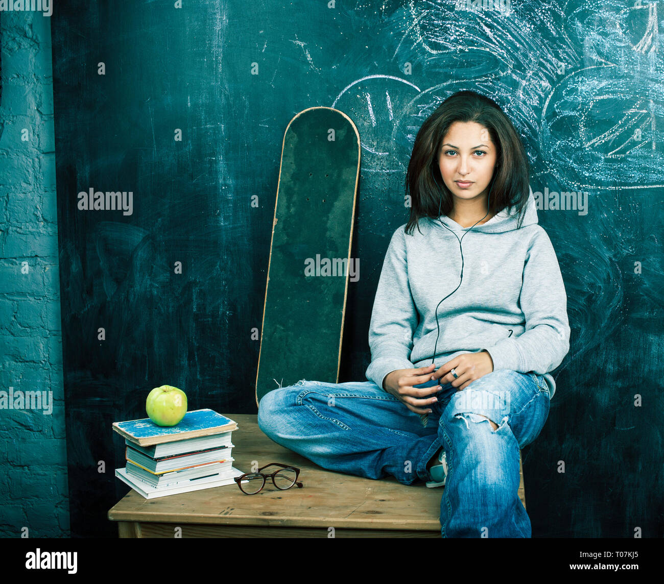 young cute teenage girl in classroom at blackboard seating on table ...