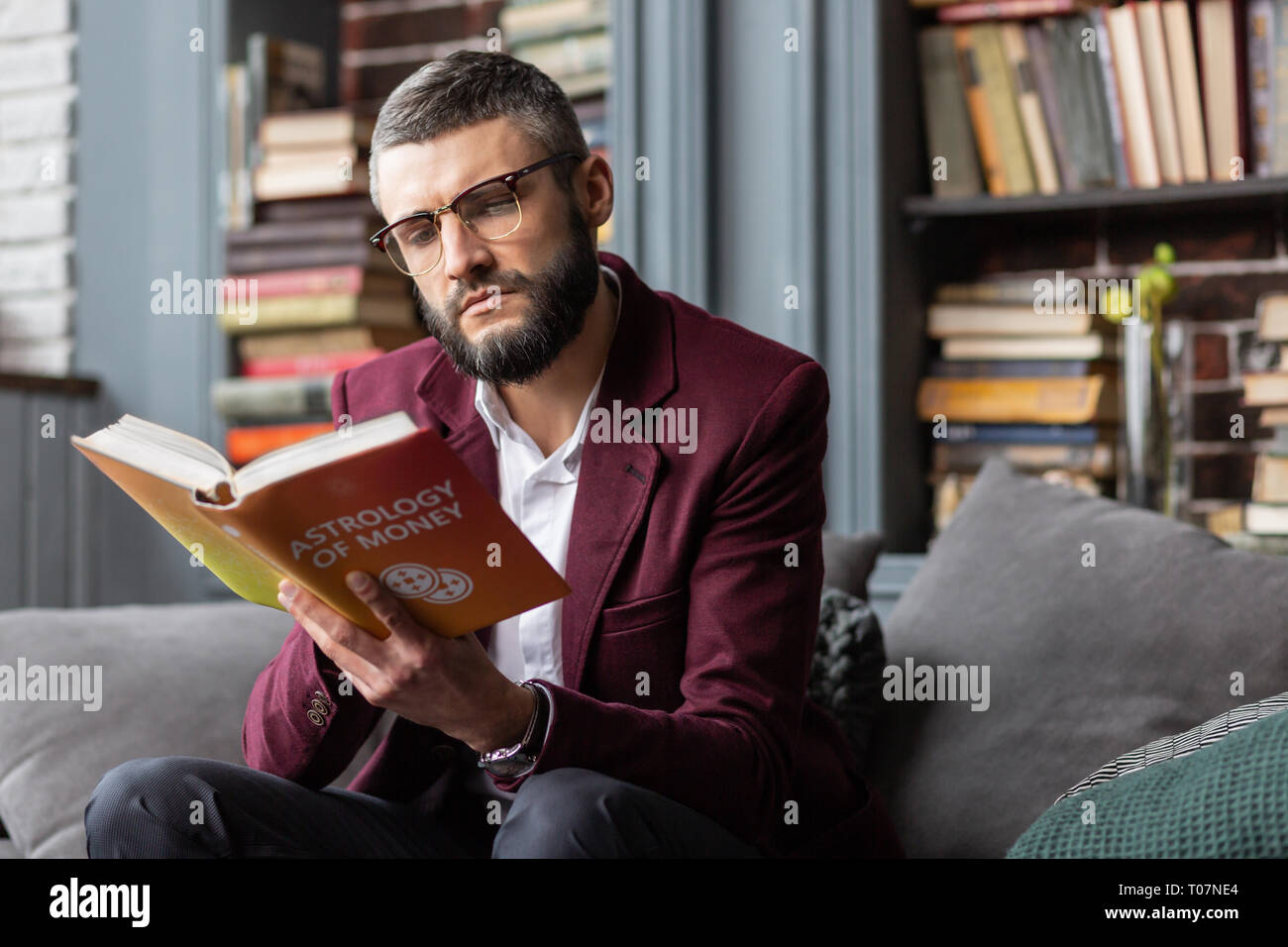 Man feeling thoughtful while reading book about astrology of money ... Man feeling thoughtful while reading book about astrology of money ...