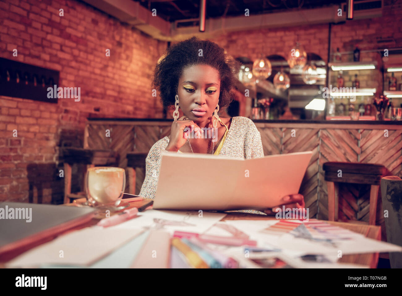 Focused alluring young woman carefully considering papers in hands ...