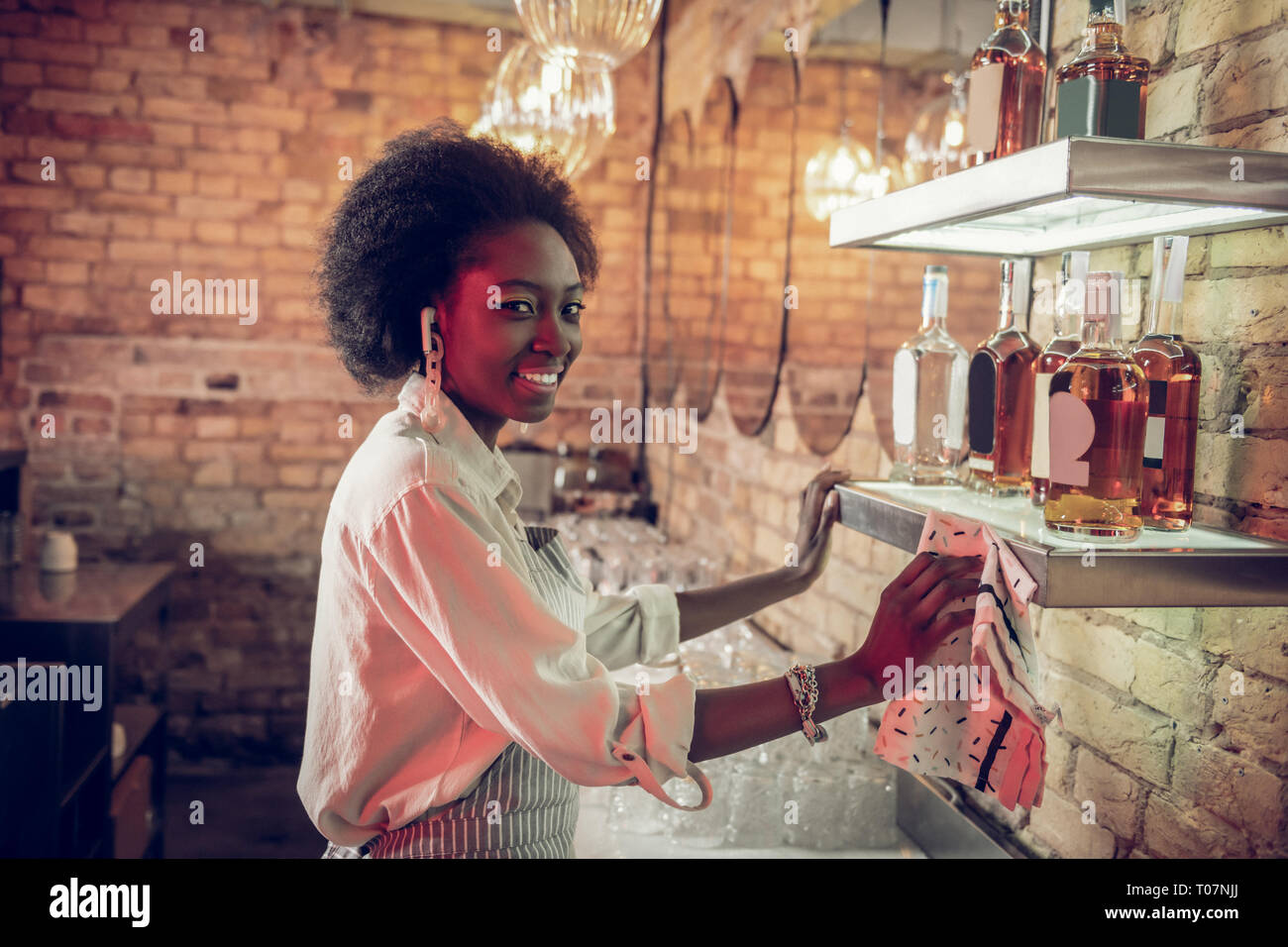 Young-adult African-American pub worker tidying up kitchen shelves with ...