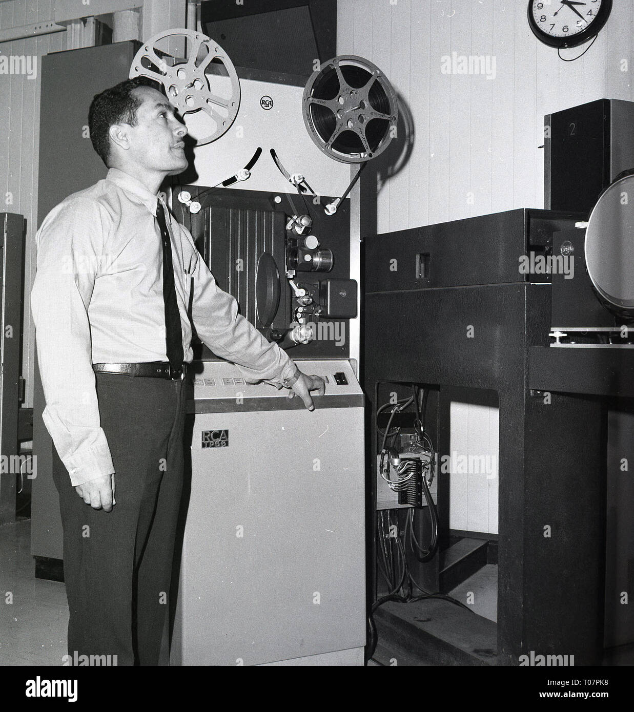 1960s, male film technician standing beside a reel to reel film machine ...
