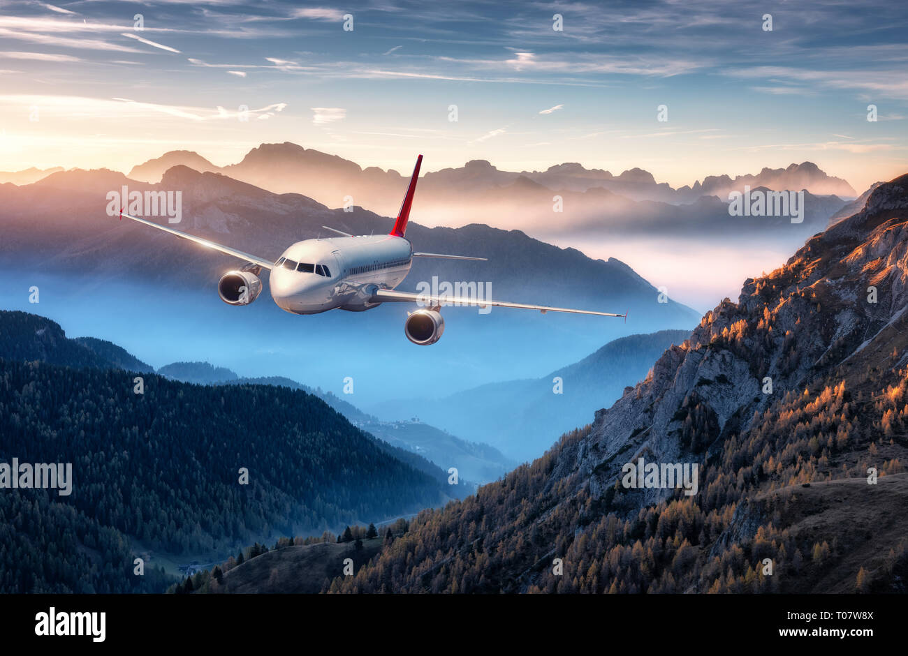 Airplane is flying over mountains in fog at colorful sunset in summer ...