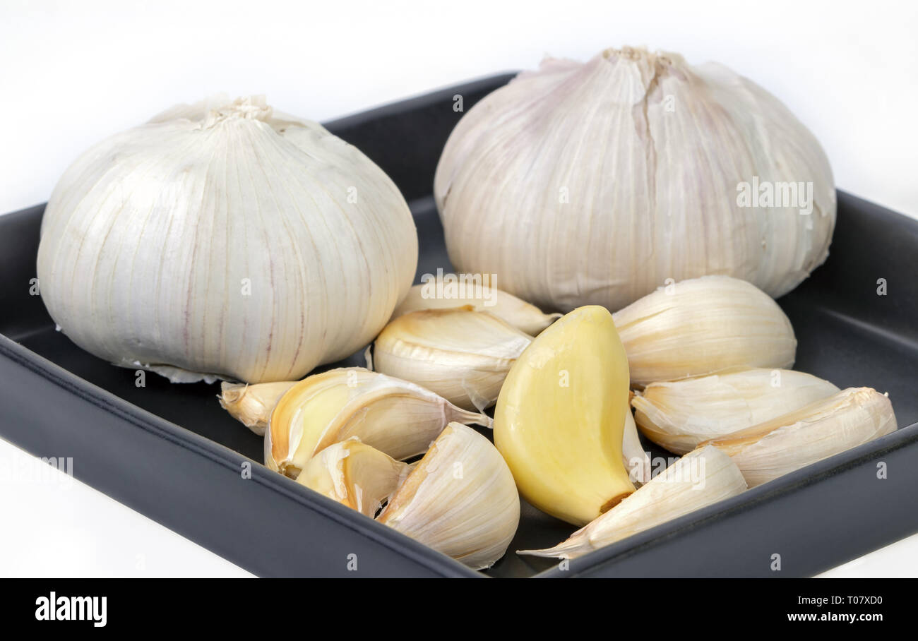 Raw and unpeeled garlic gloves on balck dish on white background Stock ...