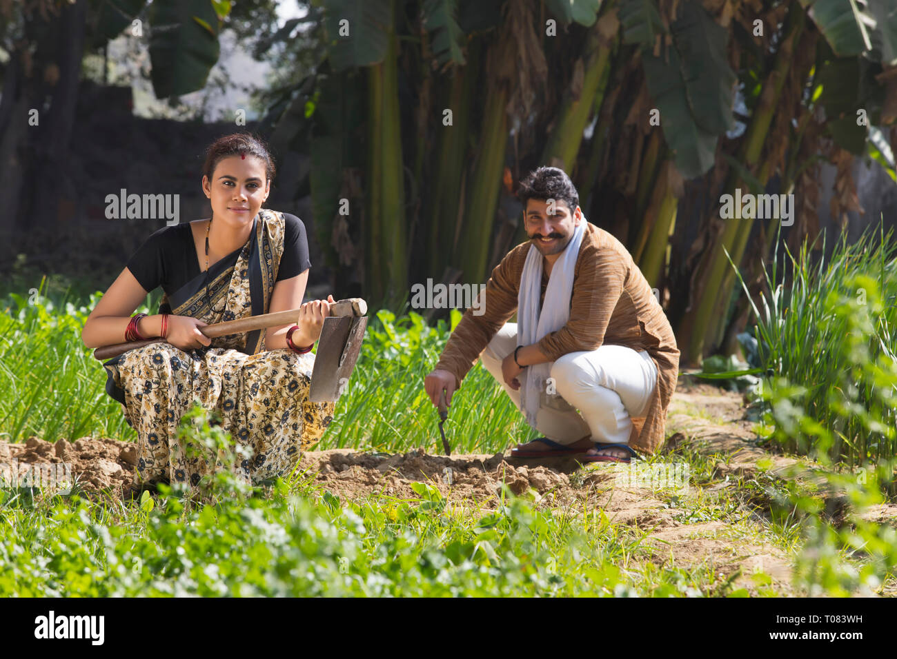Happy farmer couple working in their agriculture field holding a spade ...
