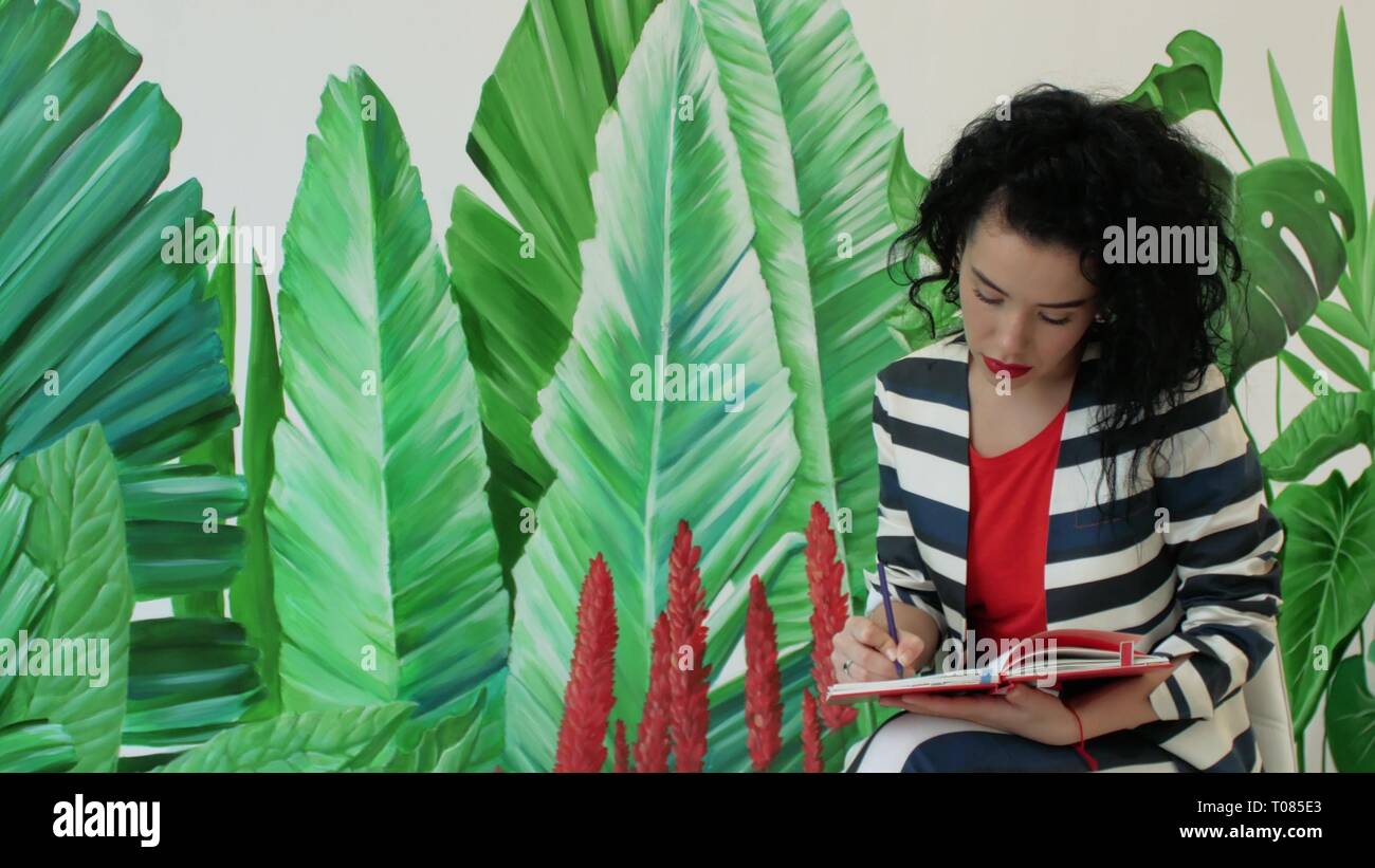 Beautiful curly woman makes notes in a notebook Stock Photo - Alamy