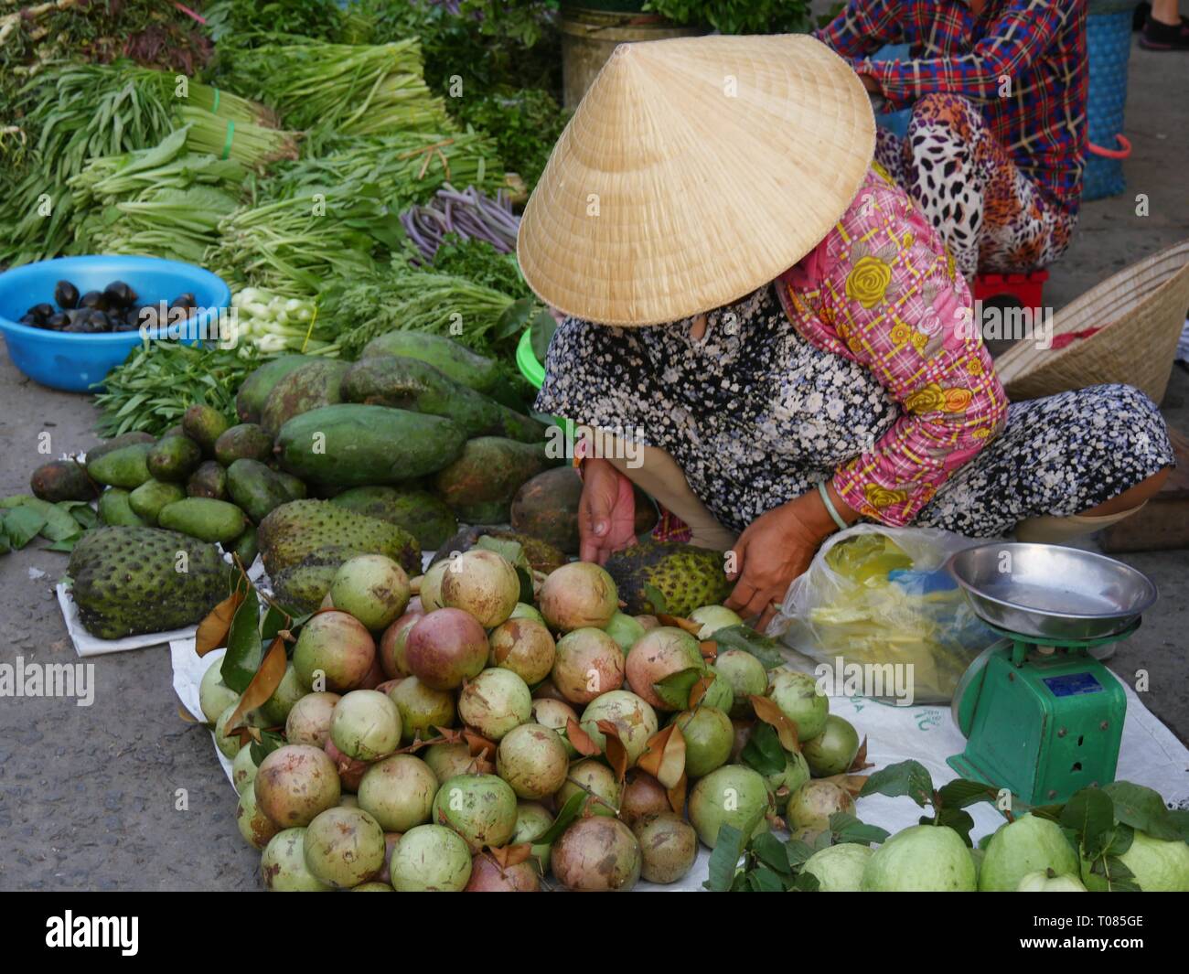 CAN THO, VIETNAM--MARCH 2018: A fruit vendor wearing a woven sits in ...