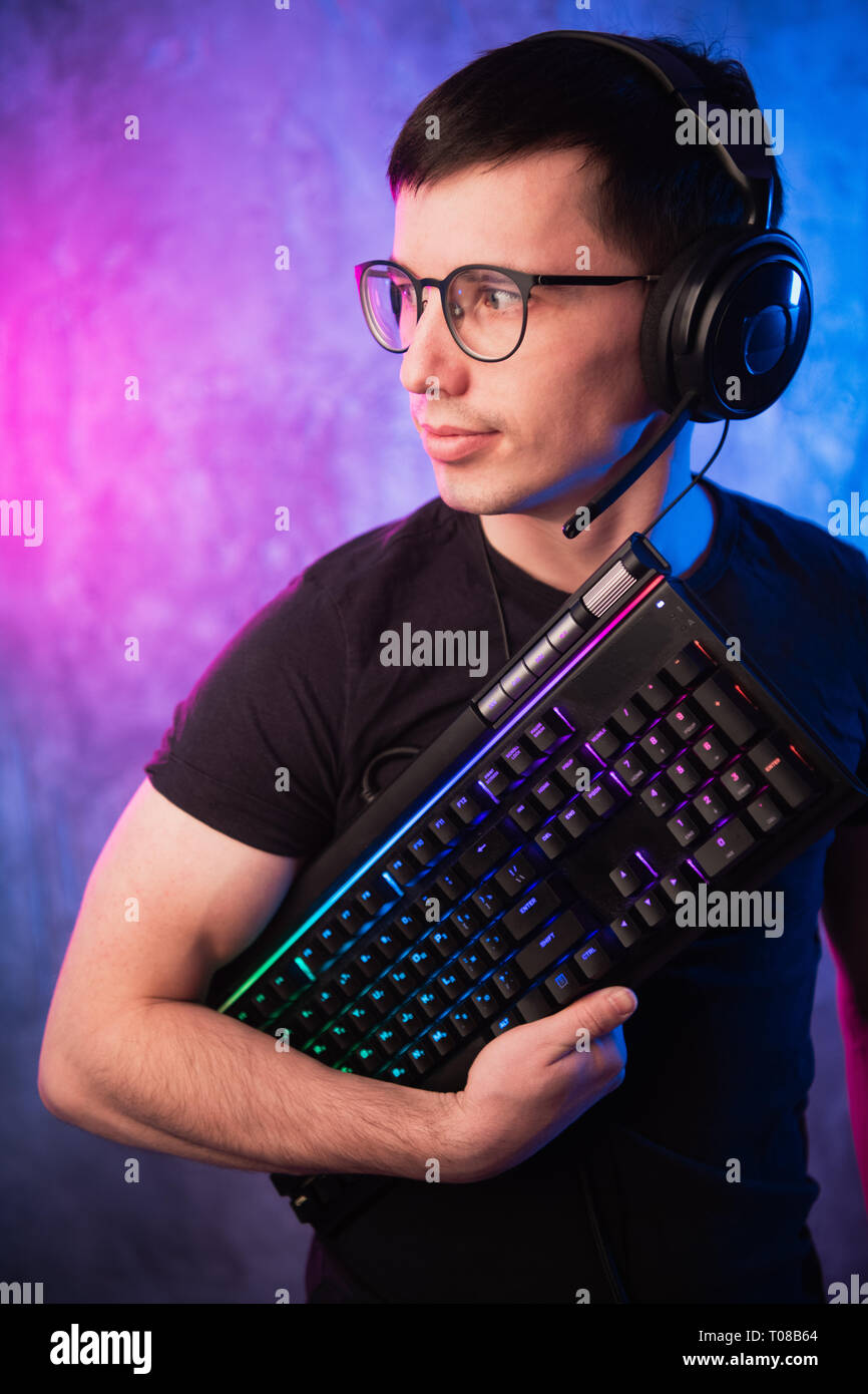 Computer nerd with keyboard over colorful pink and blue neon lit wall ...