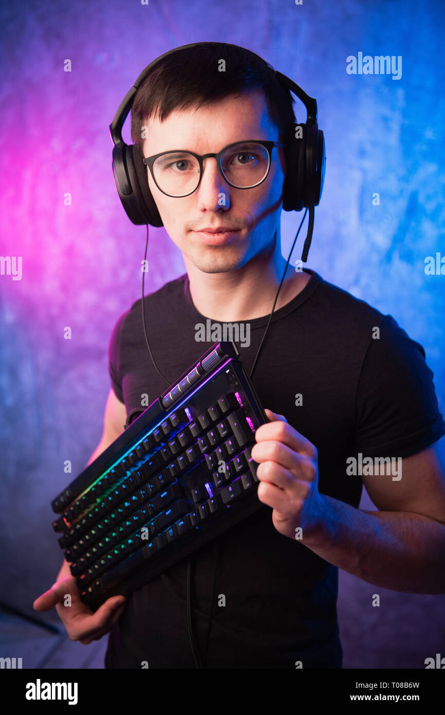Computer nerd with keyboard over colorful pink and blue neon lit wall ...
