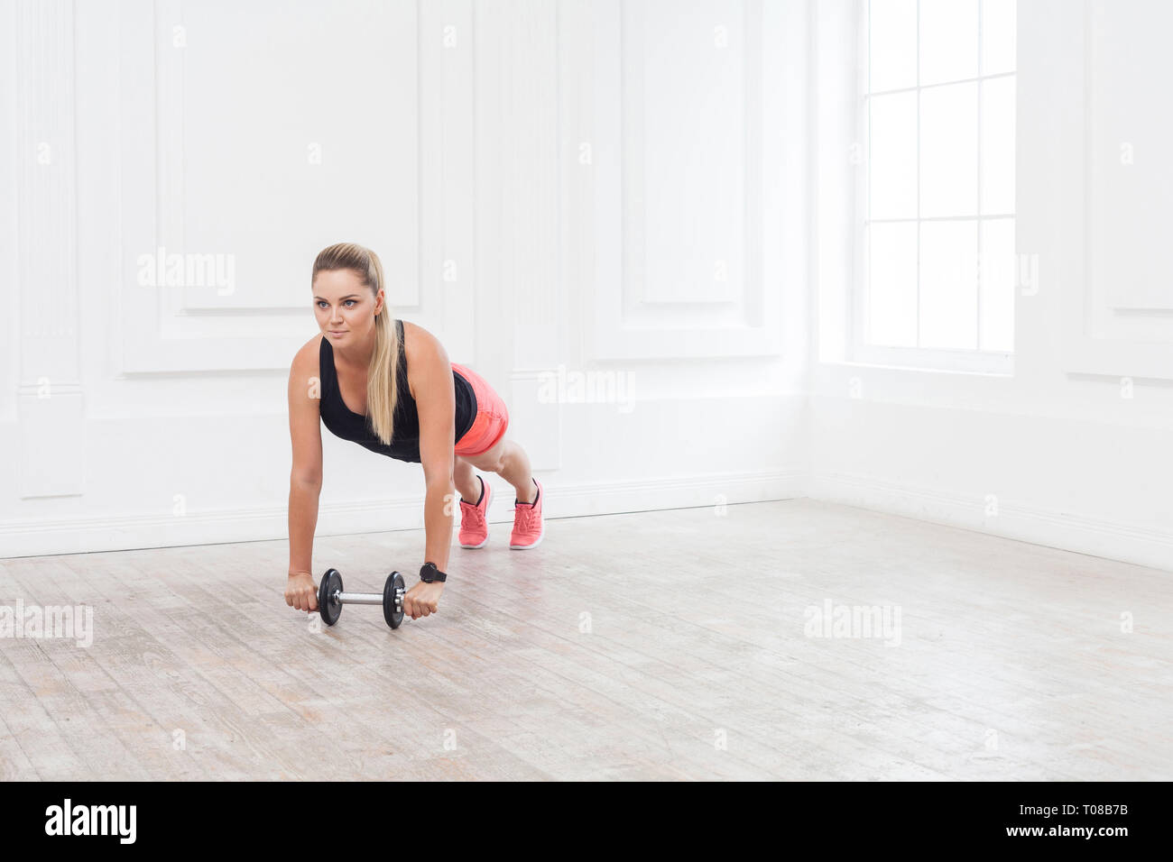 Full length portrait of athletic young woman in fit wear using dumbells ...