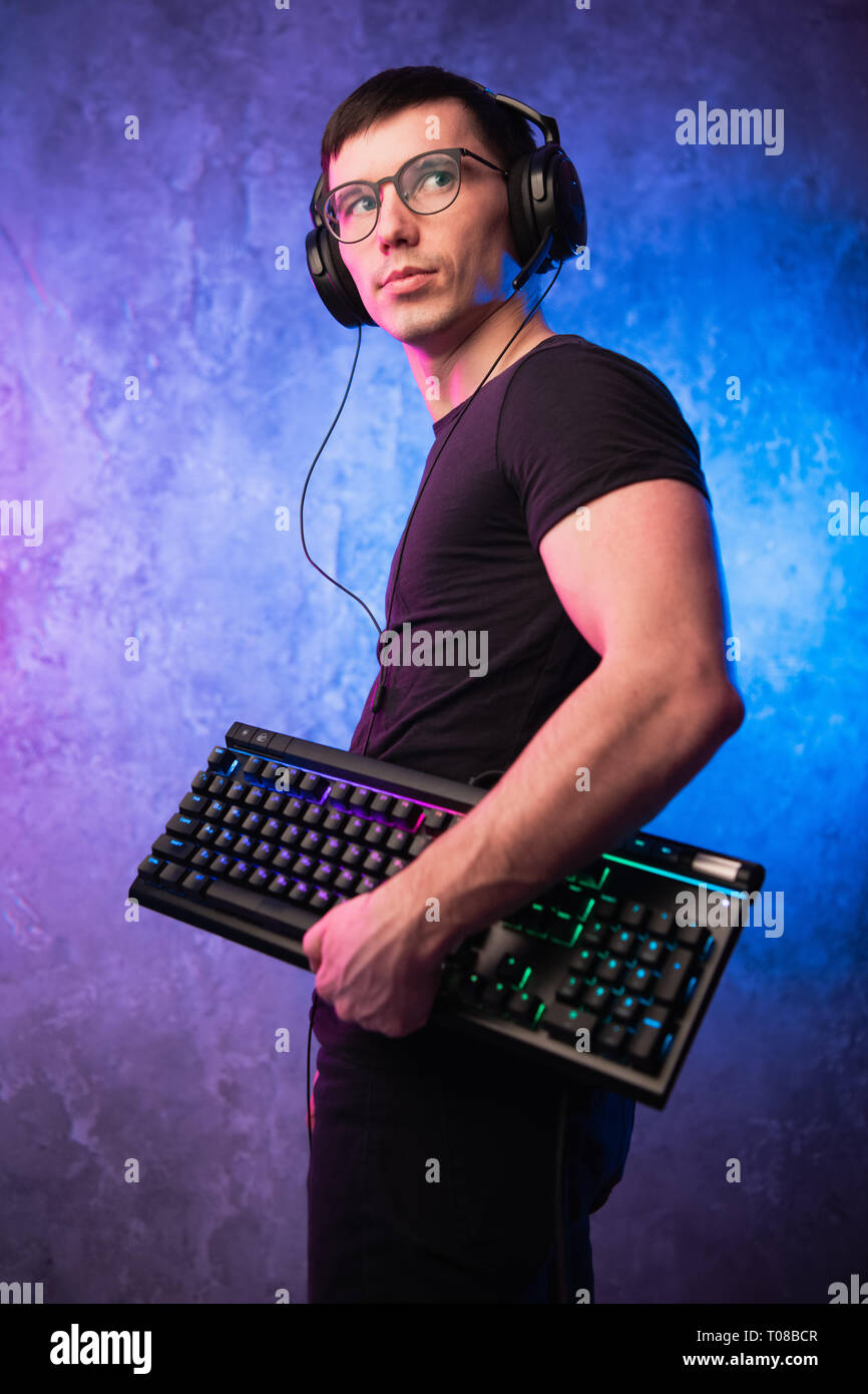 Computer nerd with keyboard over colorful pink and blue neon lit wall ...