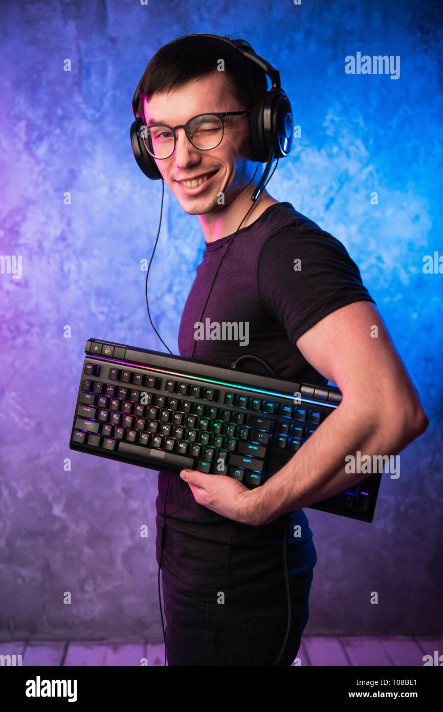 Computer nerd with keyboard over colorful pink and blue neon lit wall ...