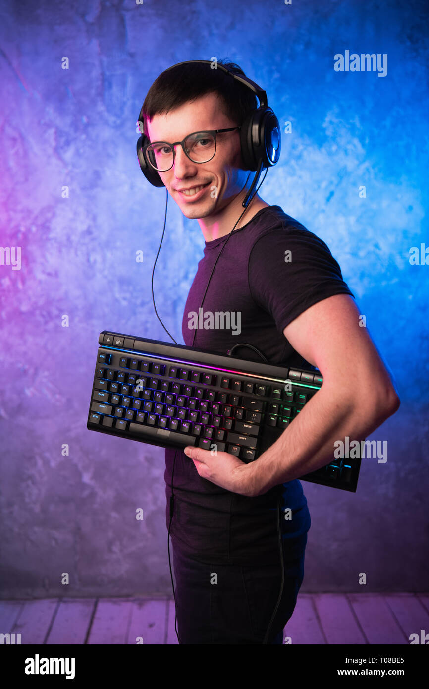 Computer nerd with keyboard over colorful pink and blue neon lit wall ...