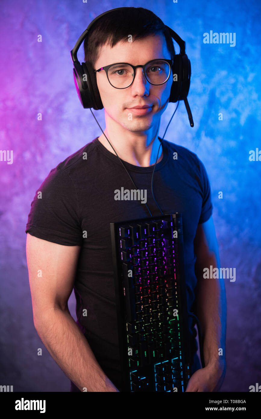 Computer nerd with keyboard over colorful pink and blue neon lit wall ...