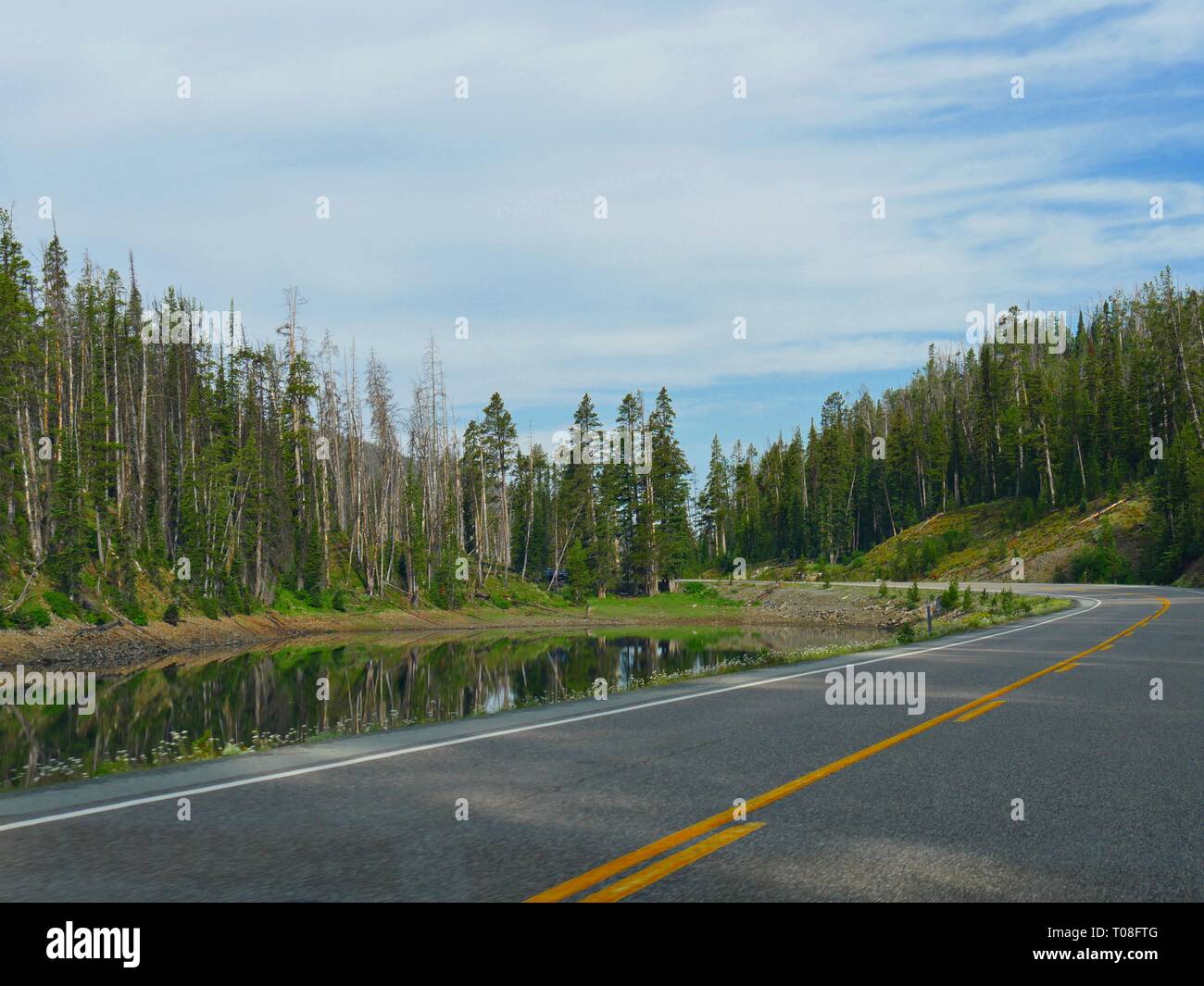 Scenic drive along a winding road with the trees reflected in the water ...
