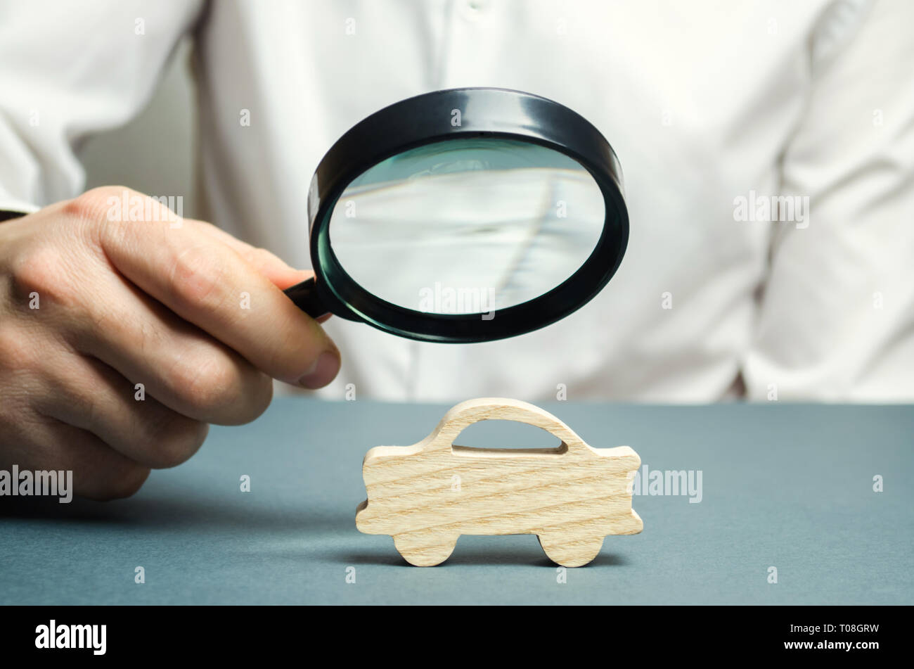A man holds a magnifying glass over a miniature wooden car. The ...
