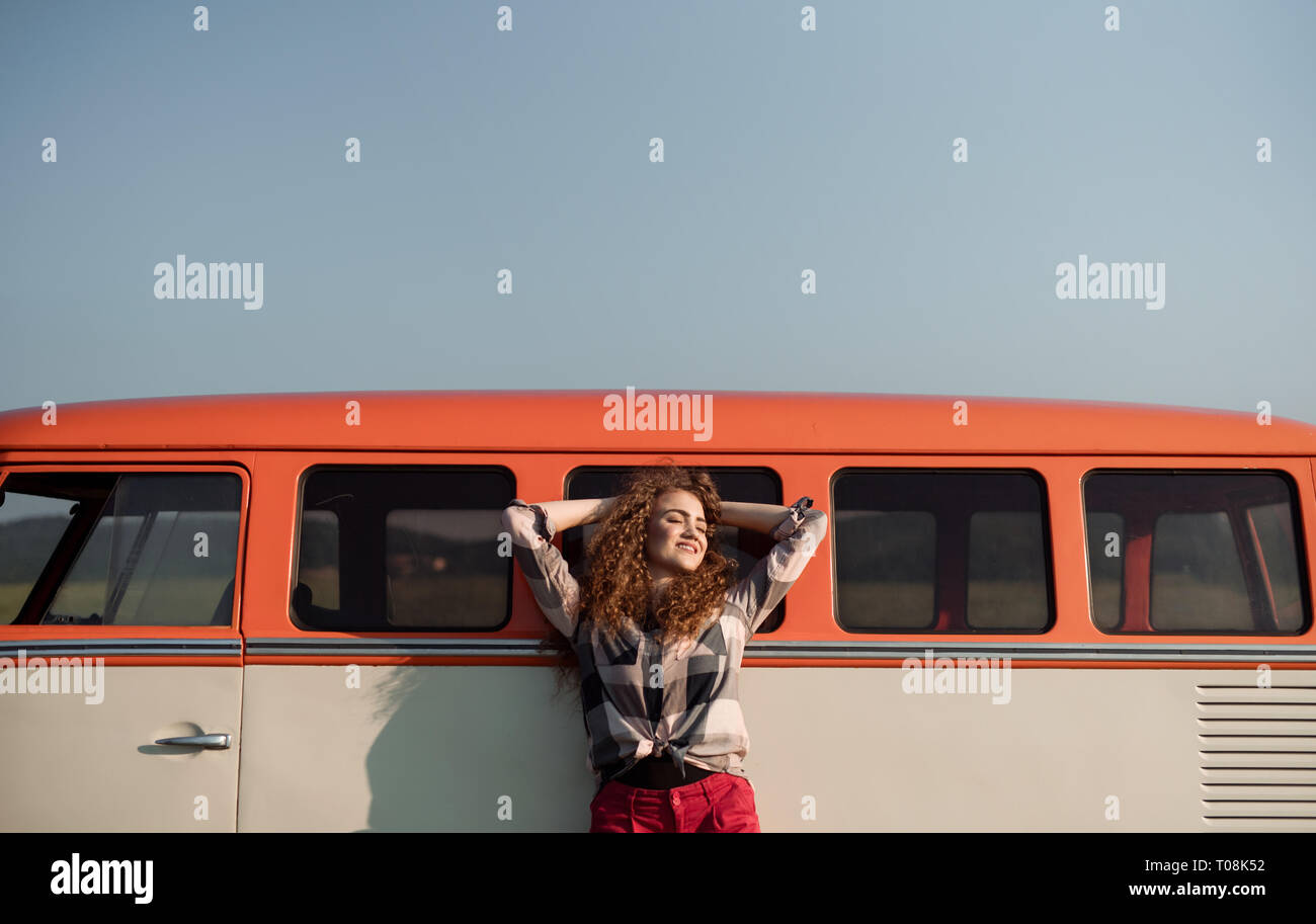 A young girl on a roadtrip through countryside, leaning on a minivan ...