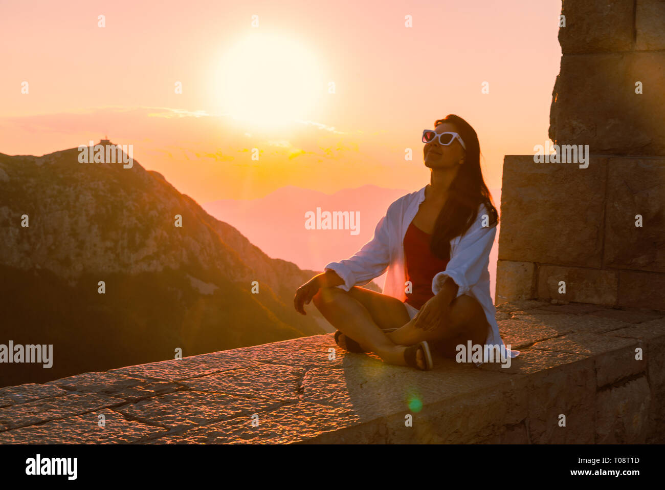 woman siting at the edge with beautiful view of sunset over mountains ...