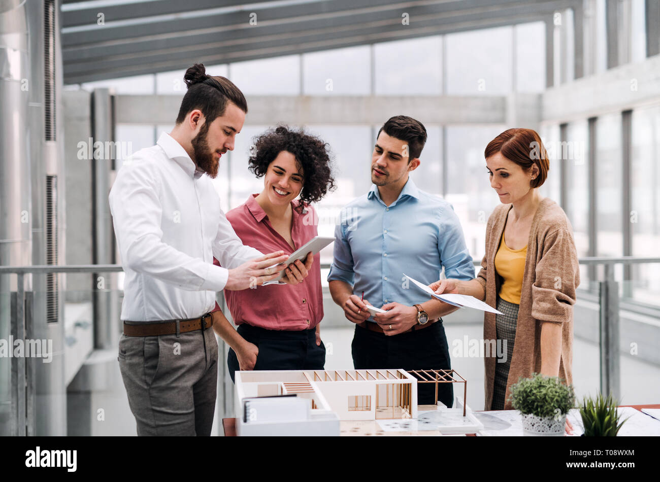 Group of young architects with model of a house standing in office ...