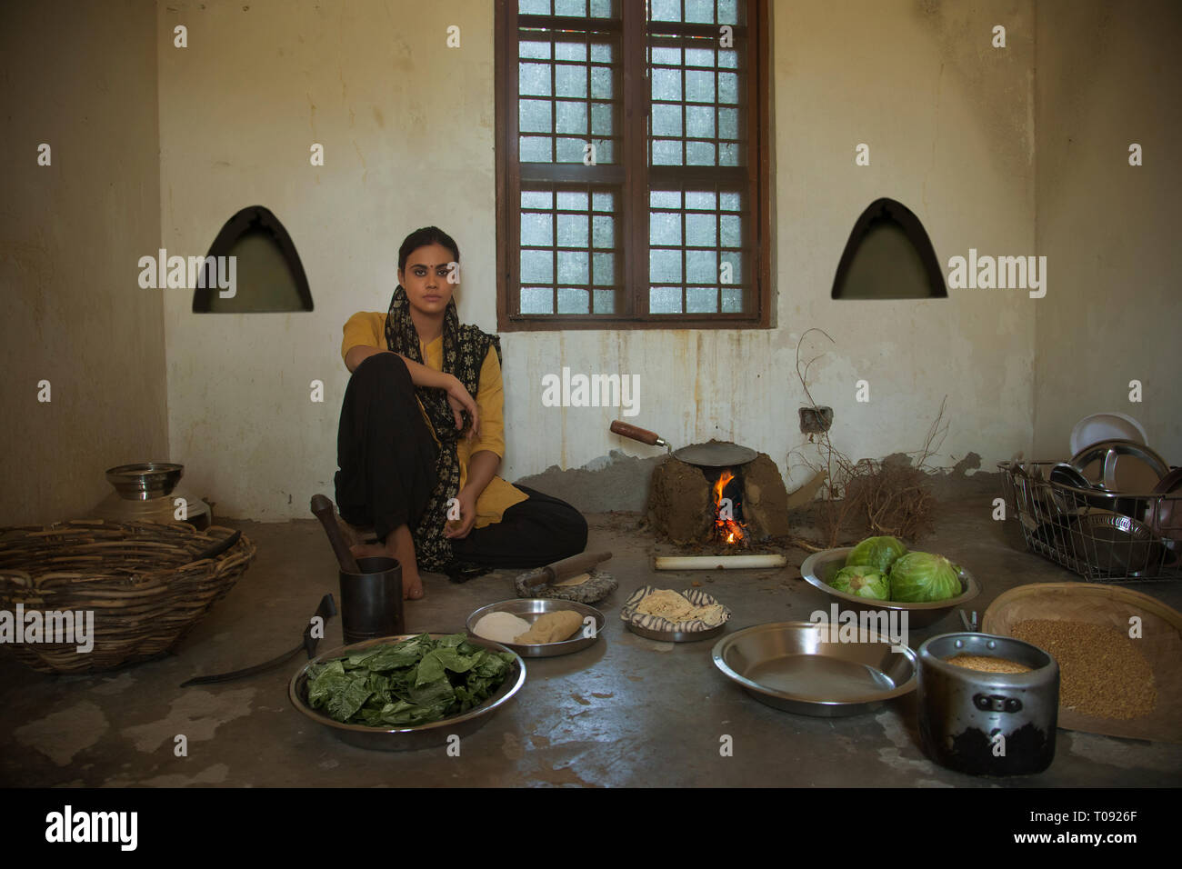 Rural woman sitting in kitchen cooking food on firewood with utensils ...