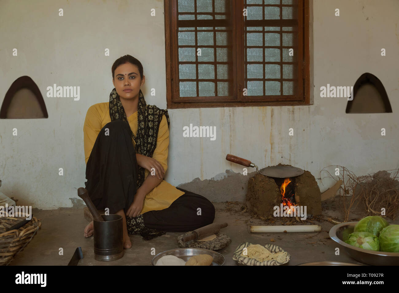 Rural woman sitting in kitchen cooking food on firewood with utensils ...